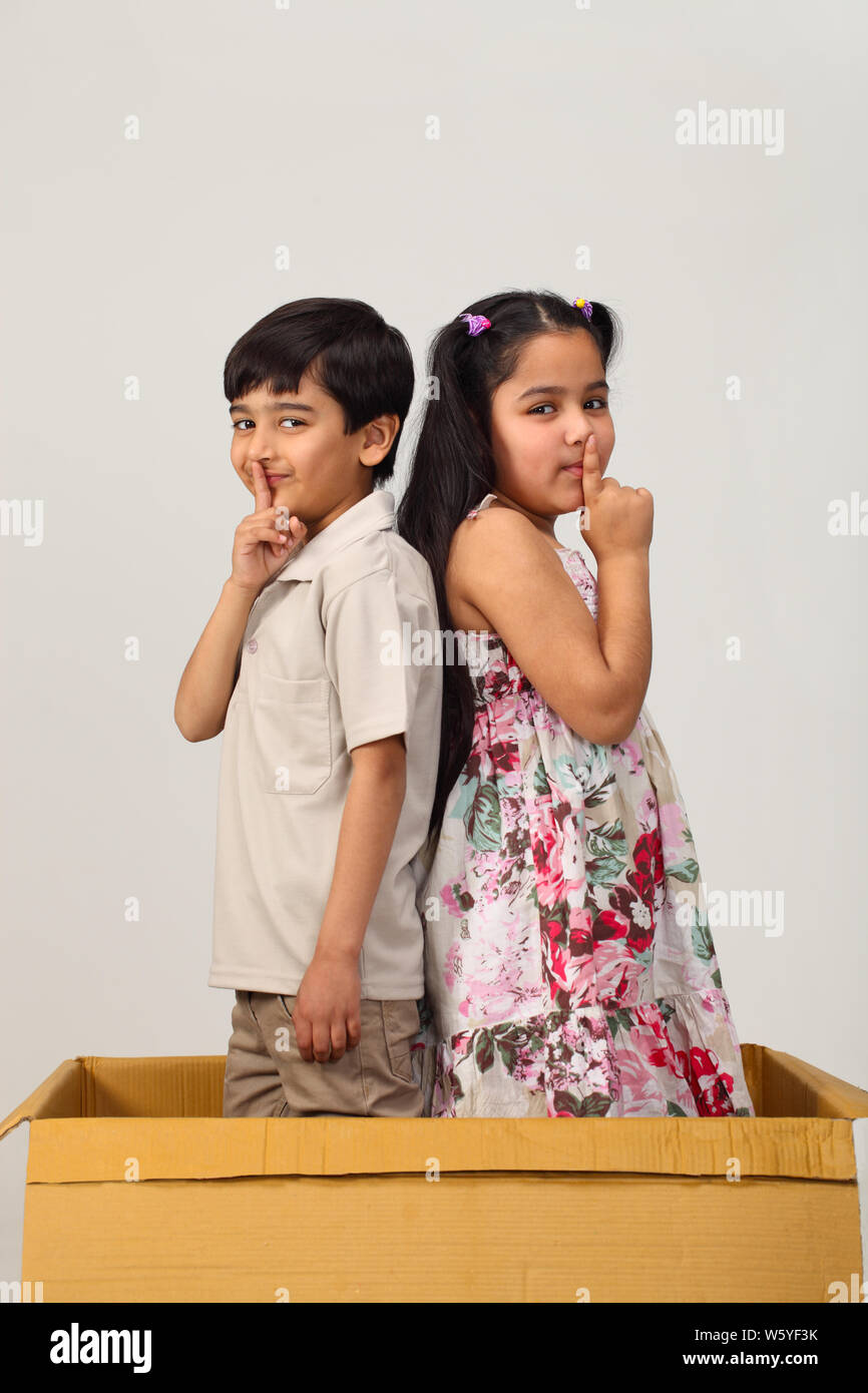 Two children standing back to back with finger on lips Stock Photo - Alamy