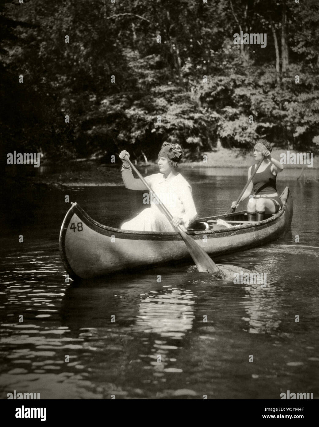 1920s TWO YOUNG WOMEN PADDLING A CANOE TOGETHER ON WOODLAND RIVER ...