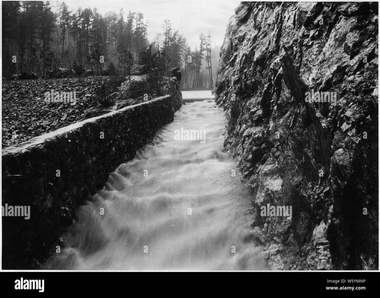 Water overflow rushing between bluff on right and stone wall on left ...