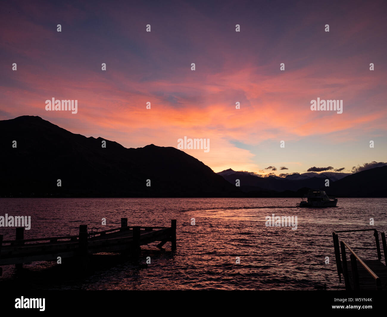 Shore of Lake Wanaka, New Zealand, at sunset with boat in silhouette ...