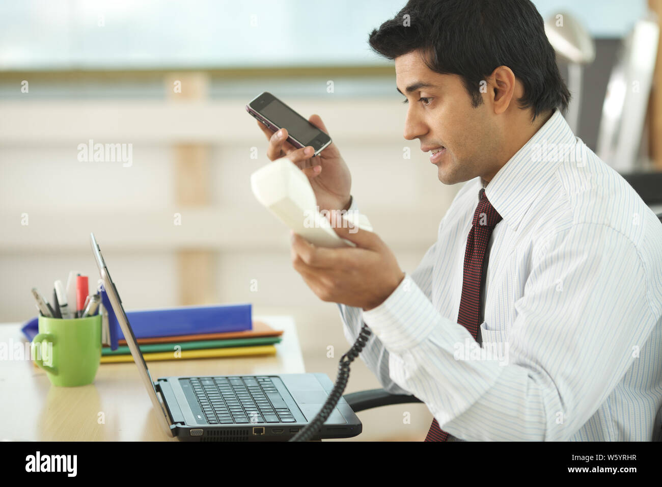 Businessman in office using cell phone and landline phone at same time ...