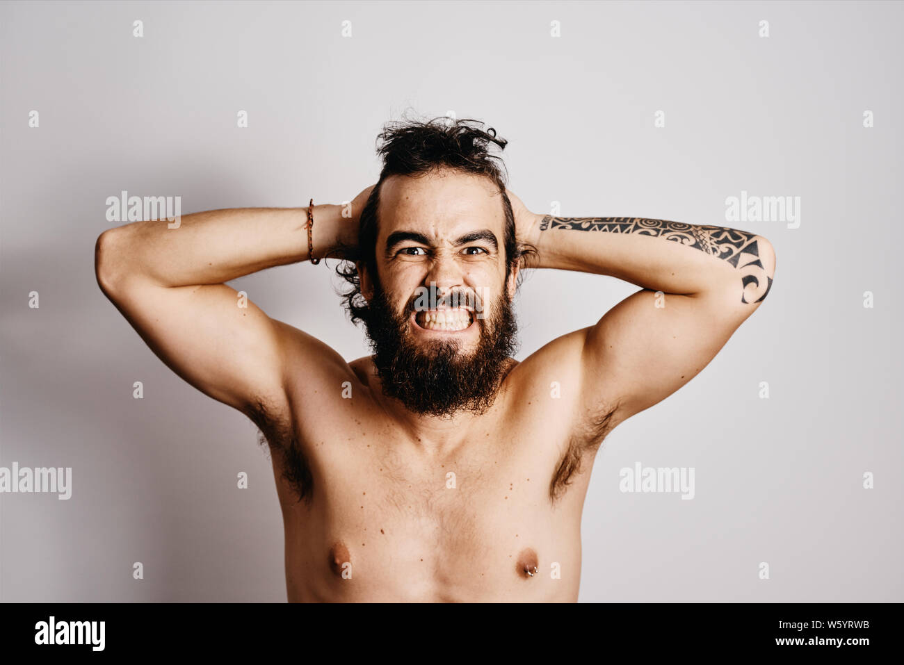 a young hipster making faces, with long hair and no shirt and tattoos ...