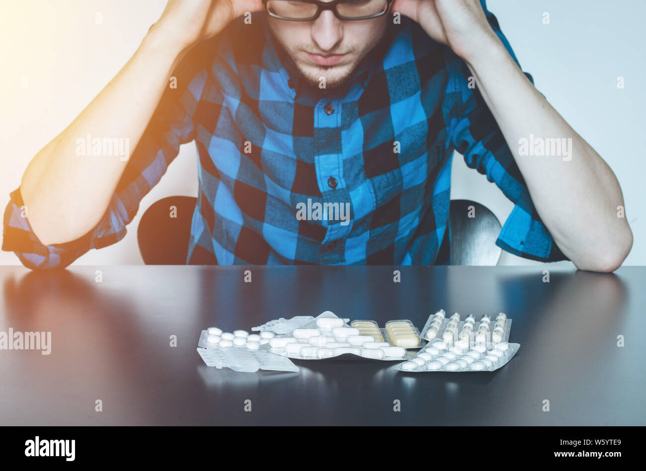 Drug abuse: Young man sitting on a table, drugs and pills in front of ...