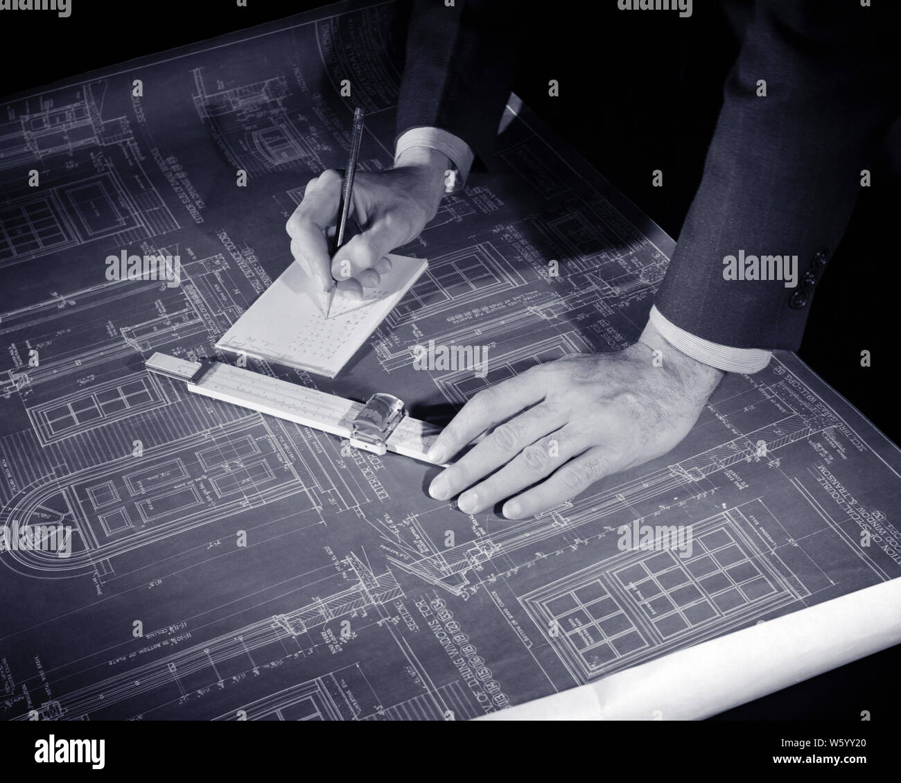 1960s MALE HANDS ON TOP OF A BLUEPRINT MAKING NOTATION ON A NOTEPAD ...