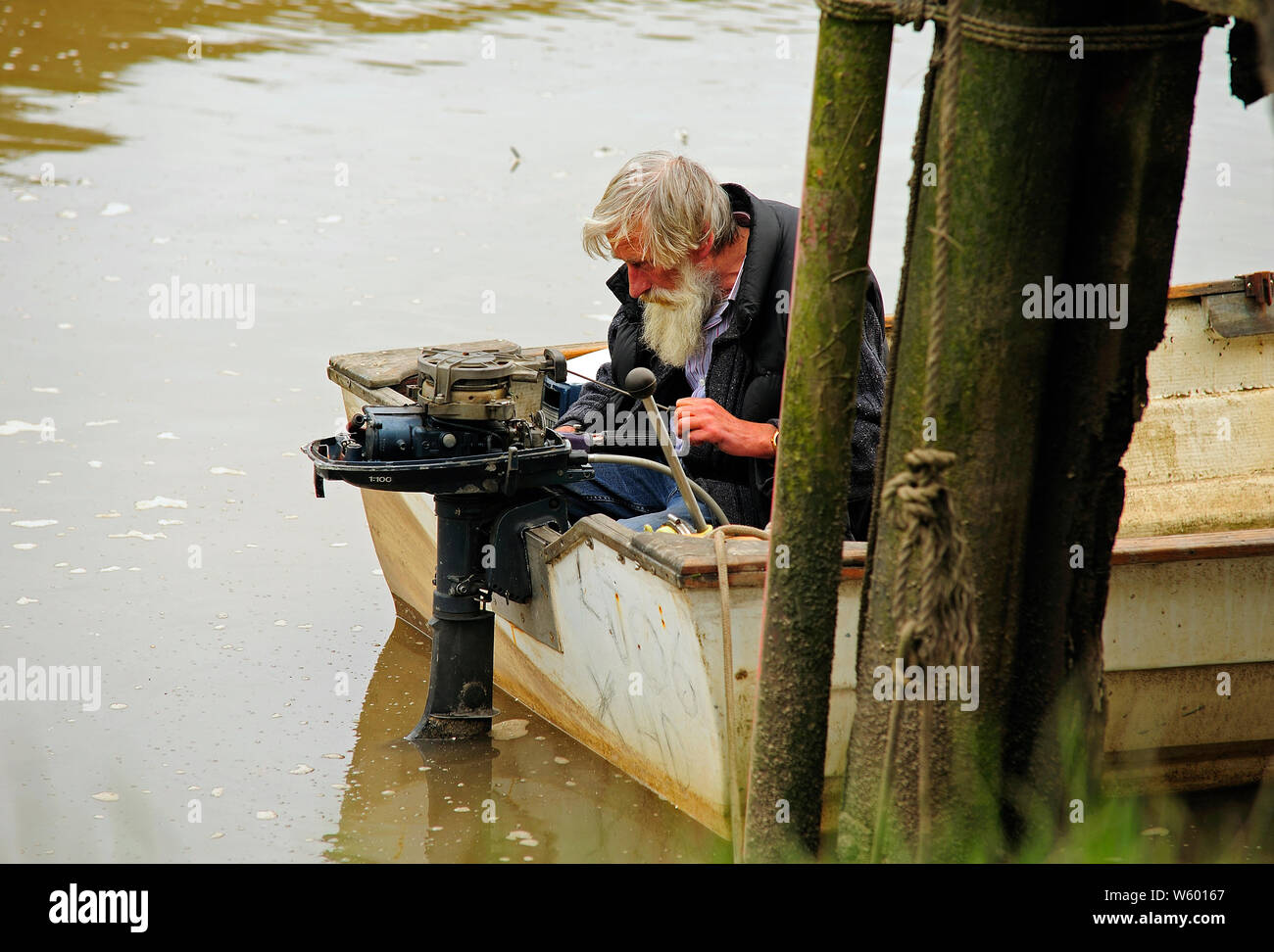 Man sat in back of small boat repairing outboard motor Stock Photo - Alamy