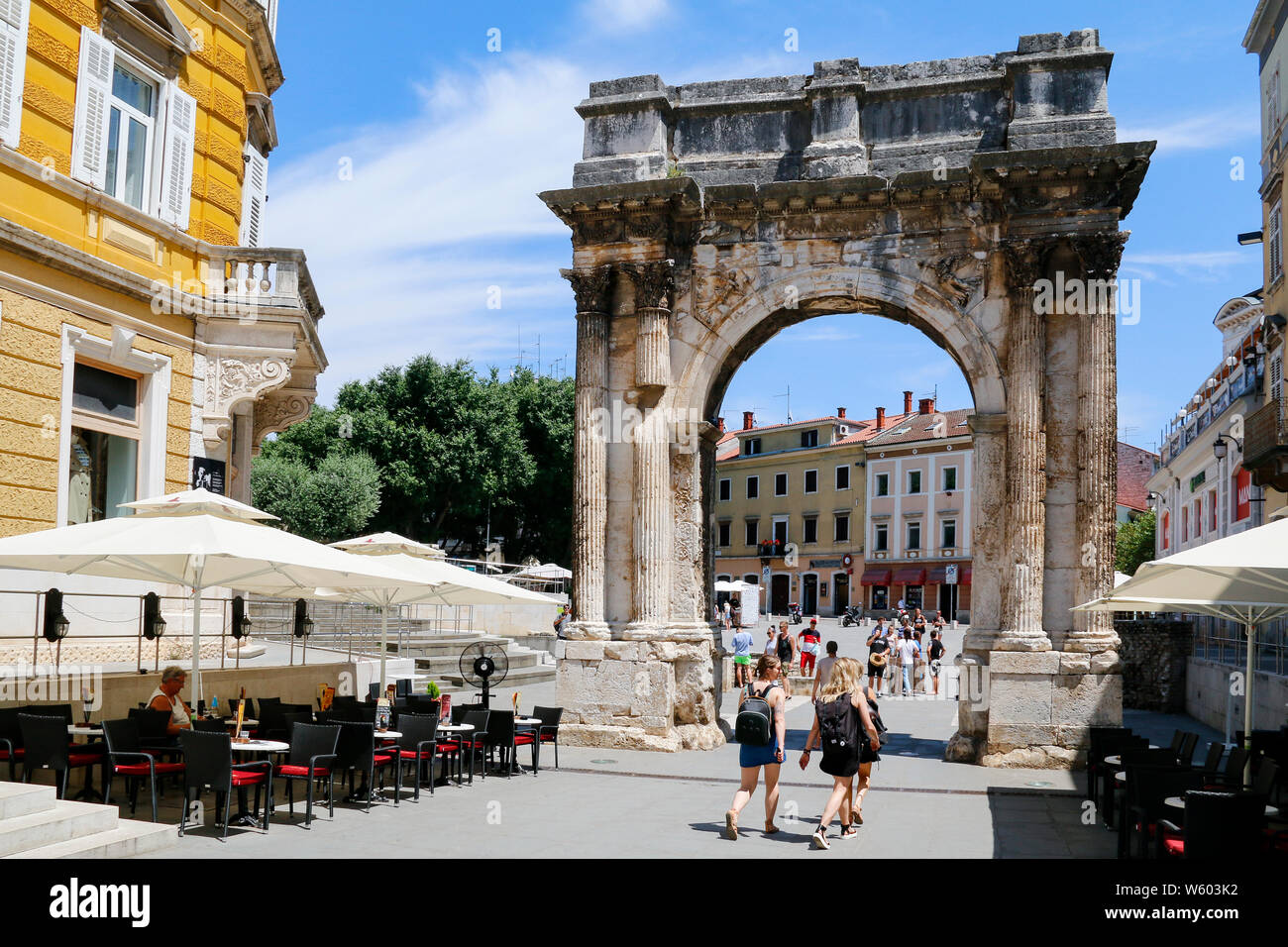 Tourists walk through the Roman Triumphal Arch of the Sergii in Pula ...
