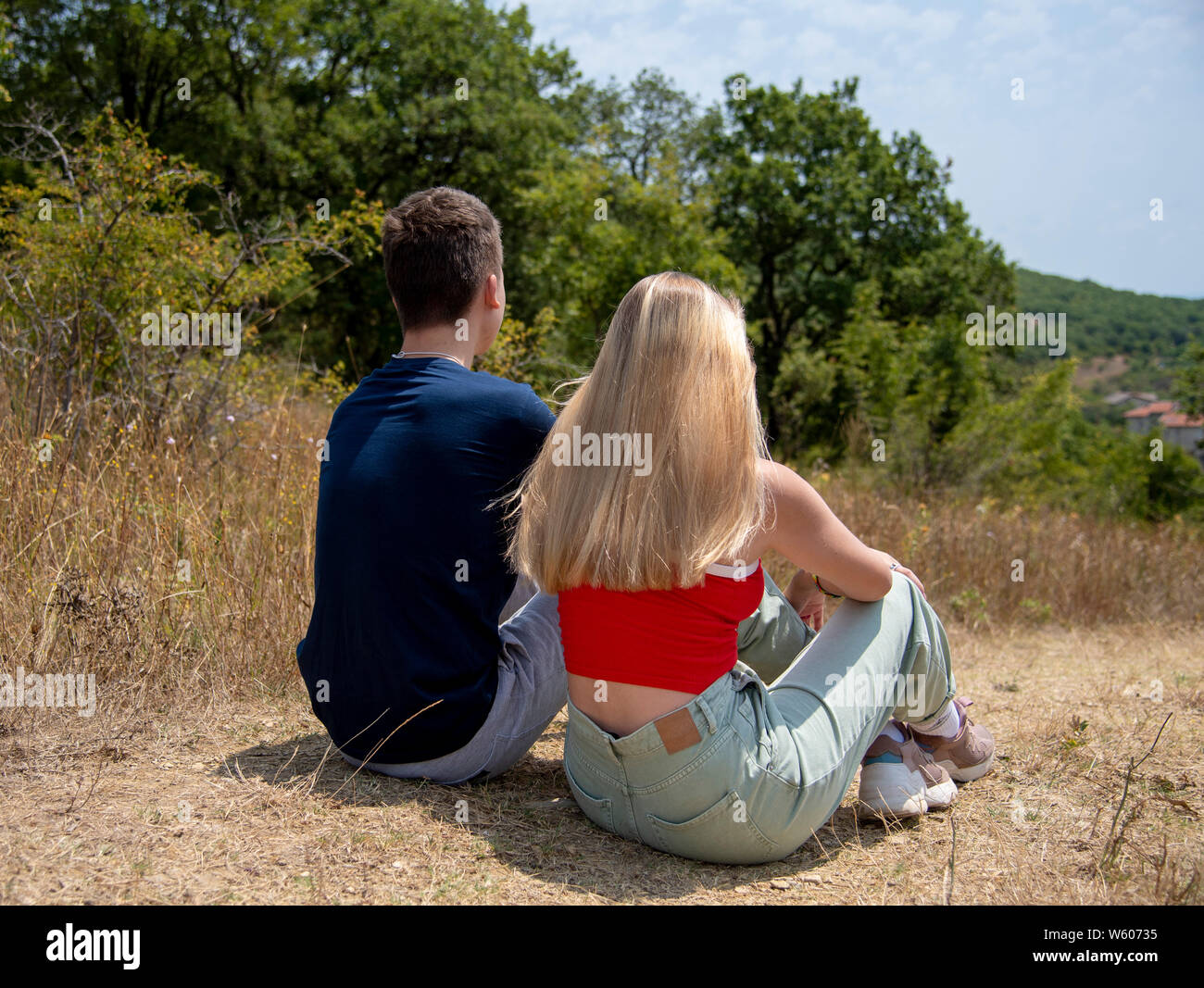 A young man and a girl are sitting on a hill on a clear sunny day and ...