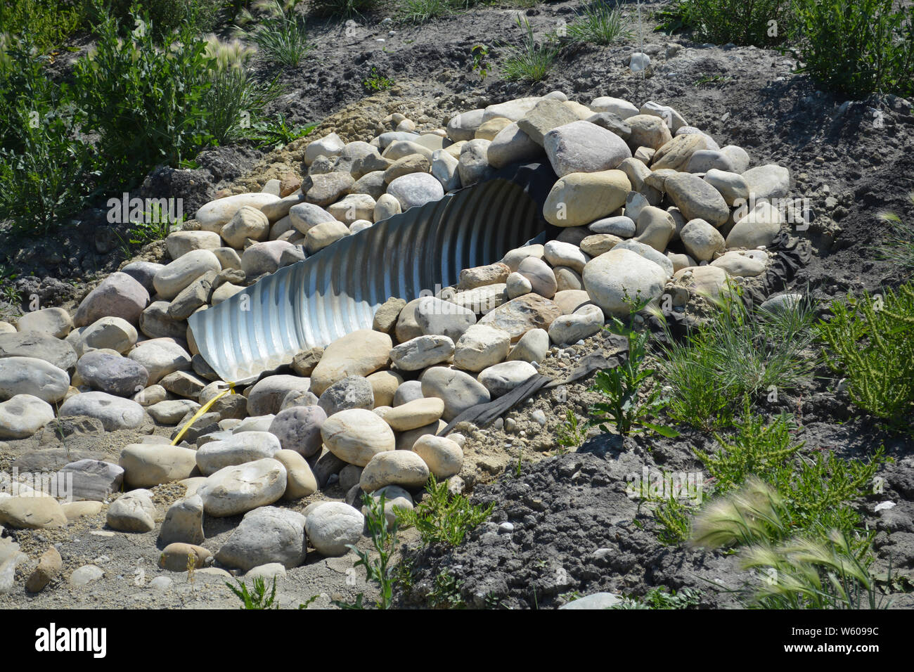 Metal drainage culvert underneath road surrounding by rocks Stock Photo ...