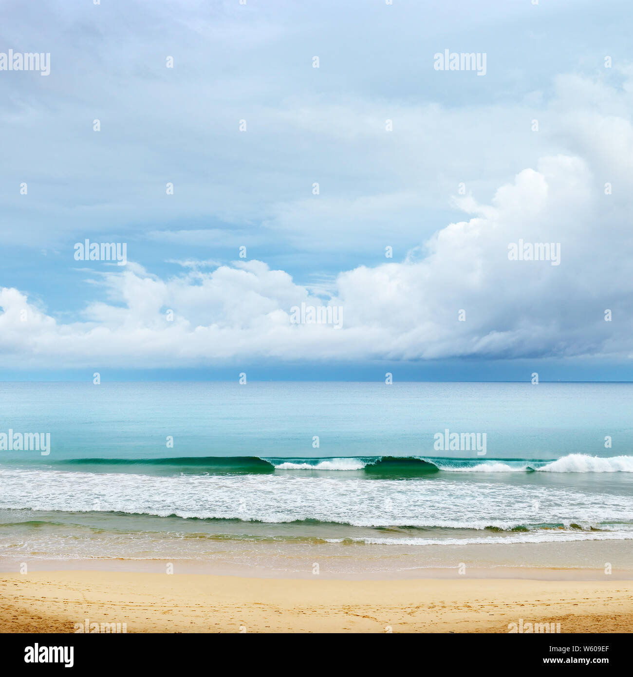 The coastline of the sandy beach, high waves and white clouds on blue ...
