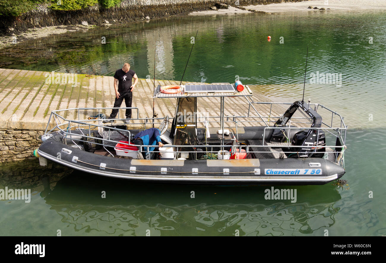 Man standing on slipway looking at a black RIB Rigid Inflatable Boat ...