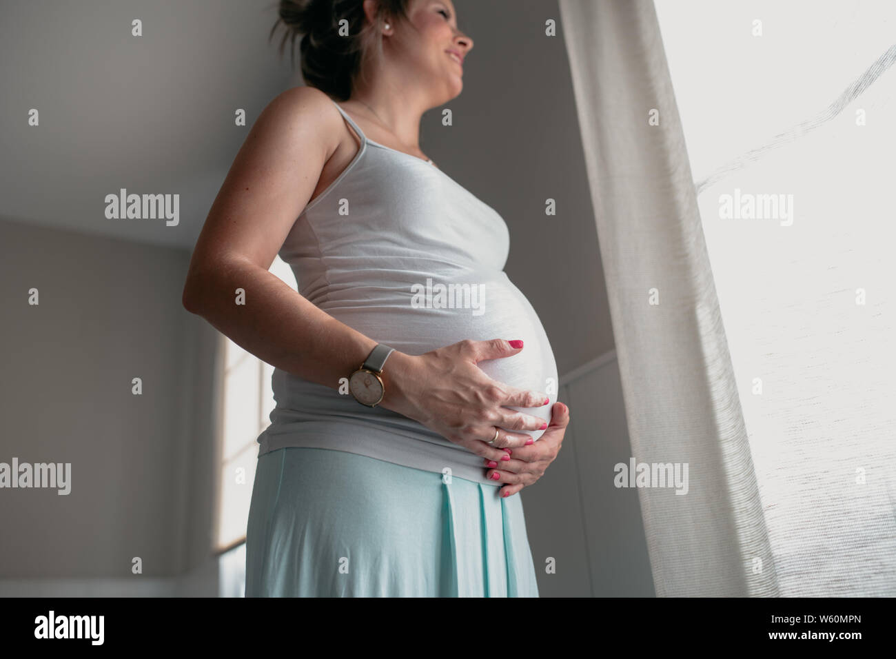 Pregnant woman looks out the window while touching her belly Stock ...