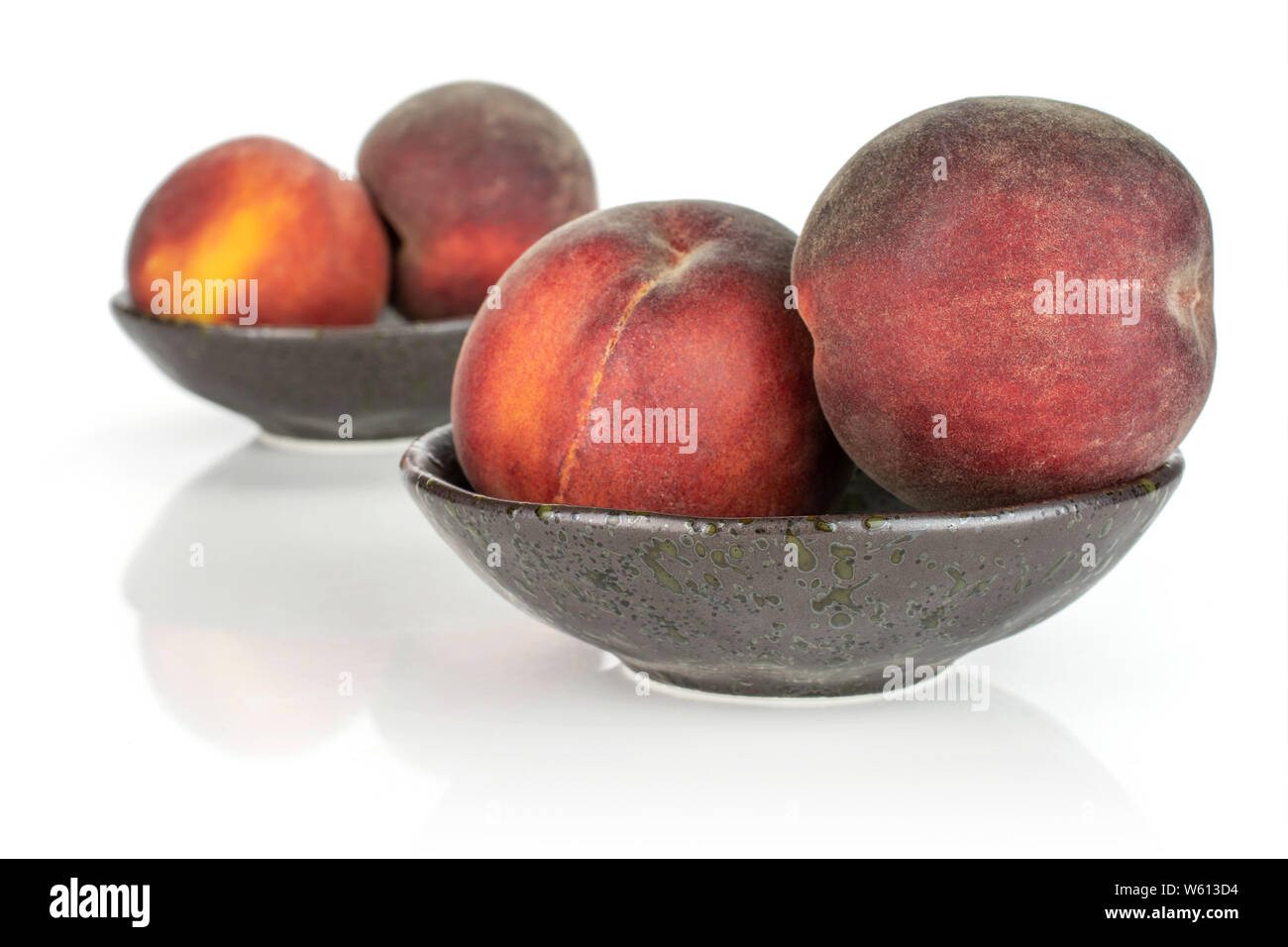 Group of four whole fresh red peach in a dark ceramic bowl isolated on ...