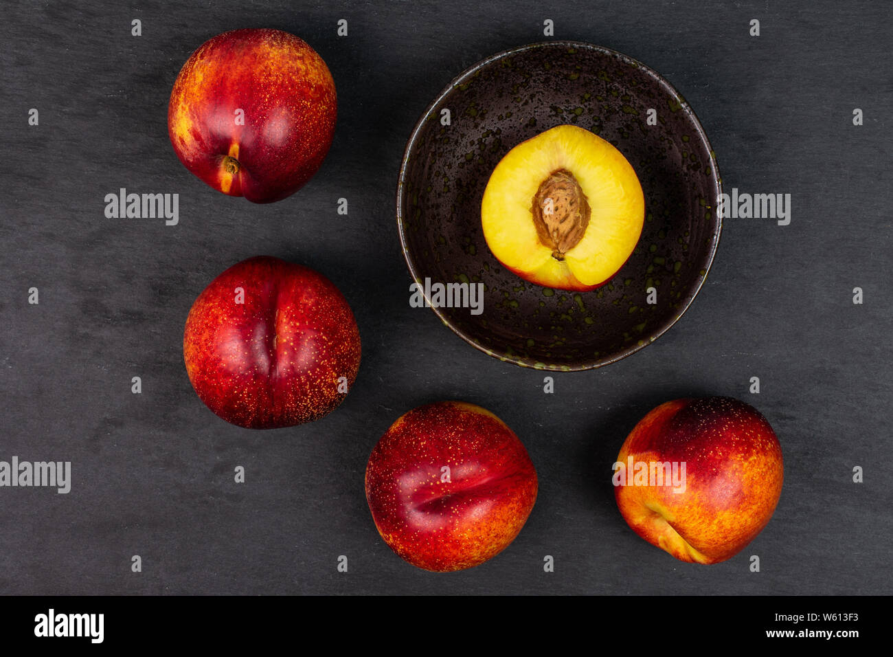 Group of four whole one half of fresh red nectarine in a dark ceramic ...