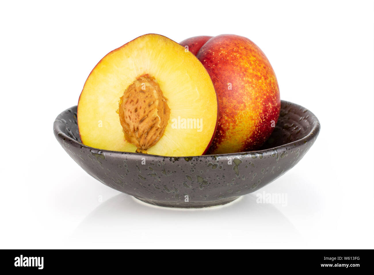 Group of one whole one half of fresh red nectarine in a dark ceramic ...