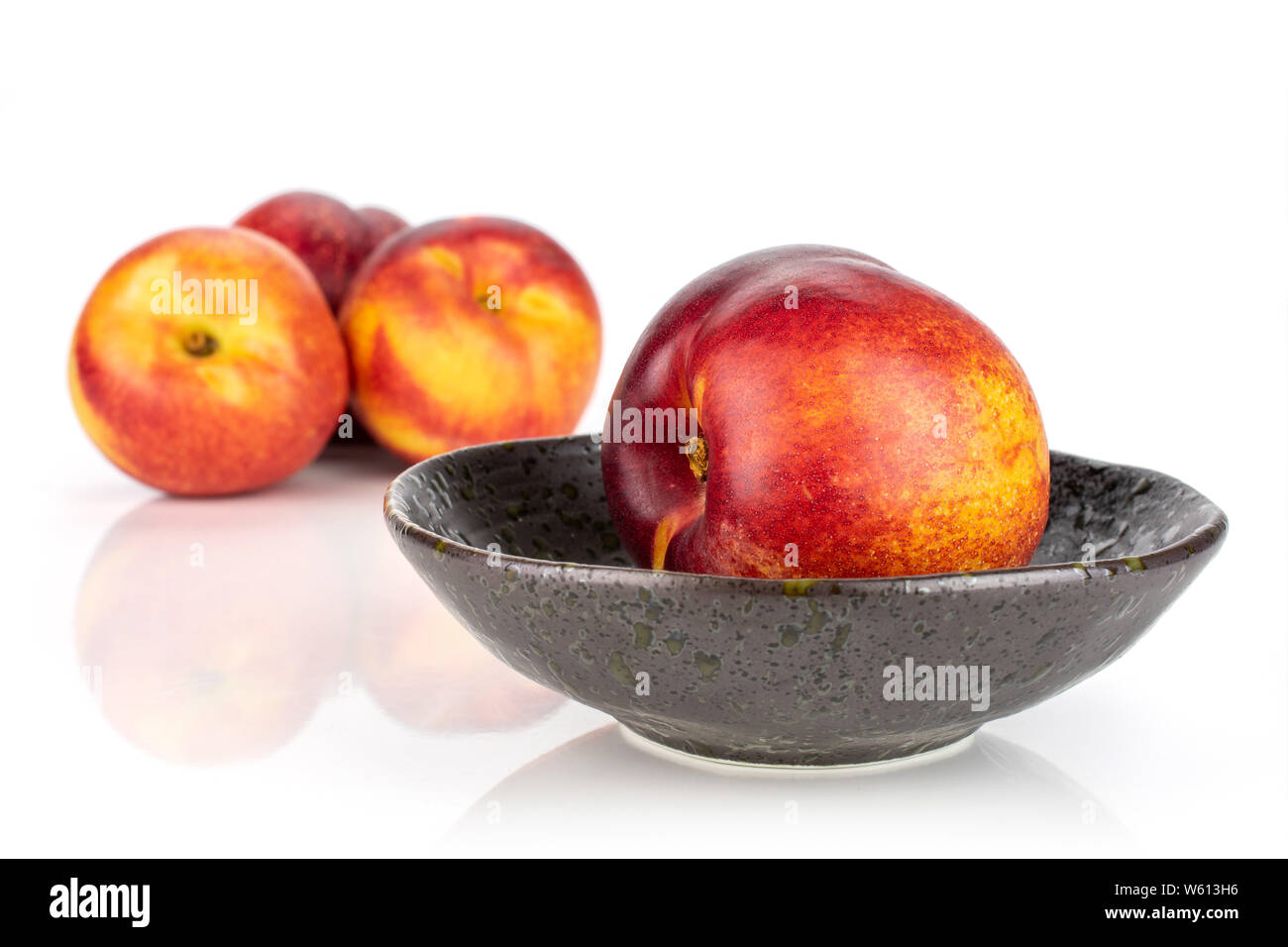 Group of four whole fresh red nectarine in a dark ceramic bowl isolated ...