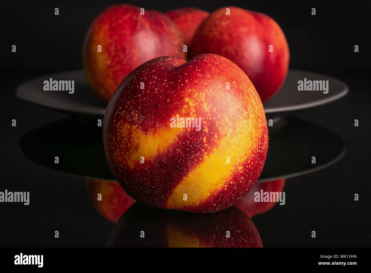 Group of four whole fresh red nectarine on a gray ceramic plate ...