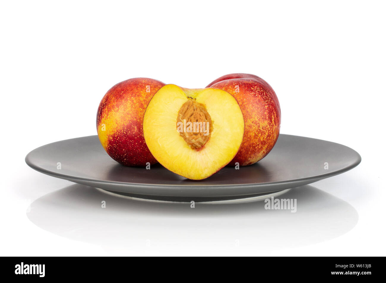 Group of two whole one half of fresh red nectarine on a gray ceramic ...