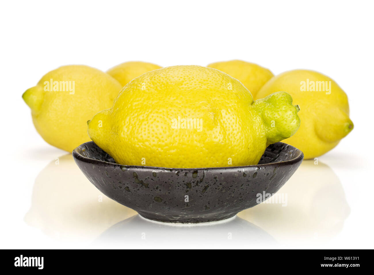 Group of five whole fresh yellow lemon in a dark ceramic bowl isolated ...
