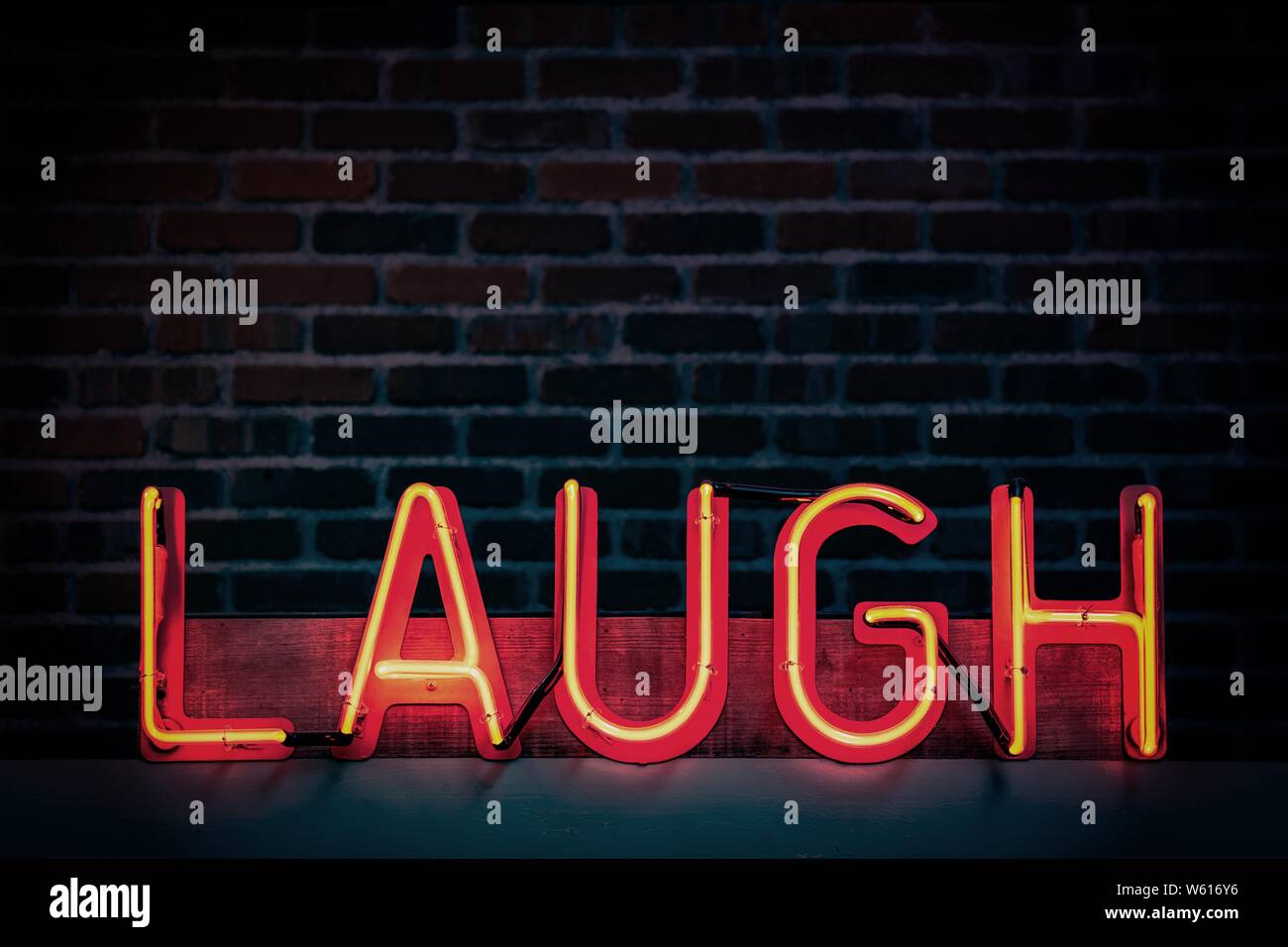 Red neon sign that says "LAUGH" on a dark brick wall background Stock ...