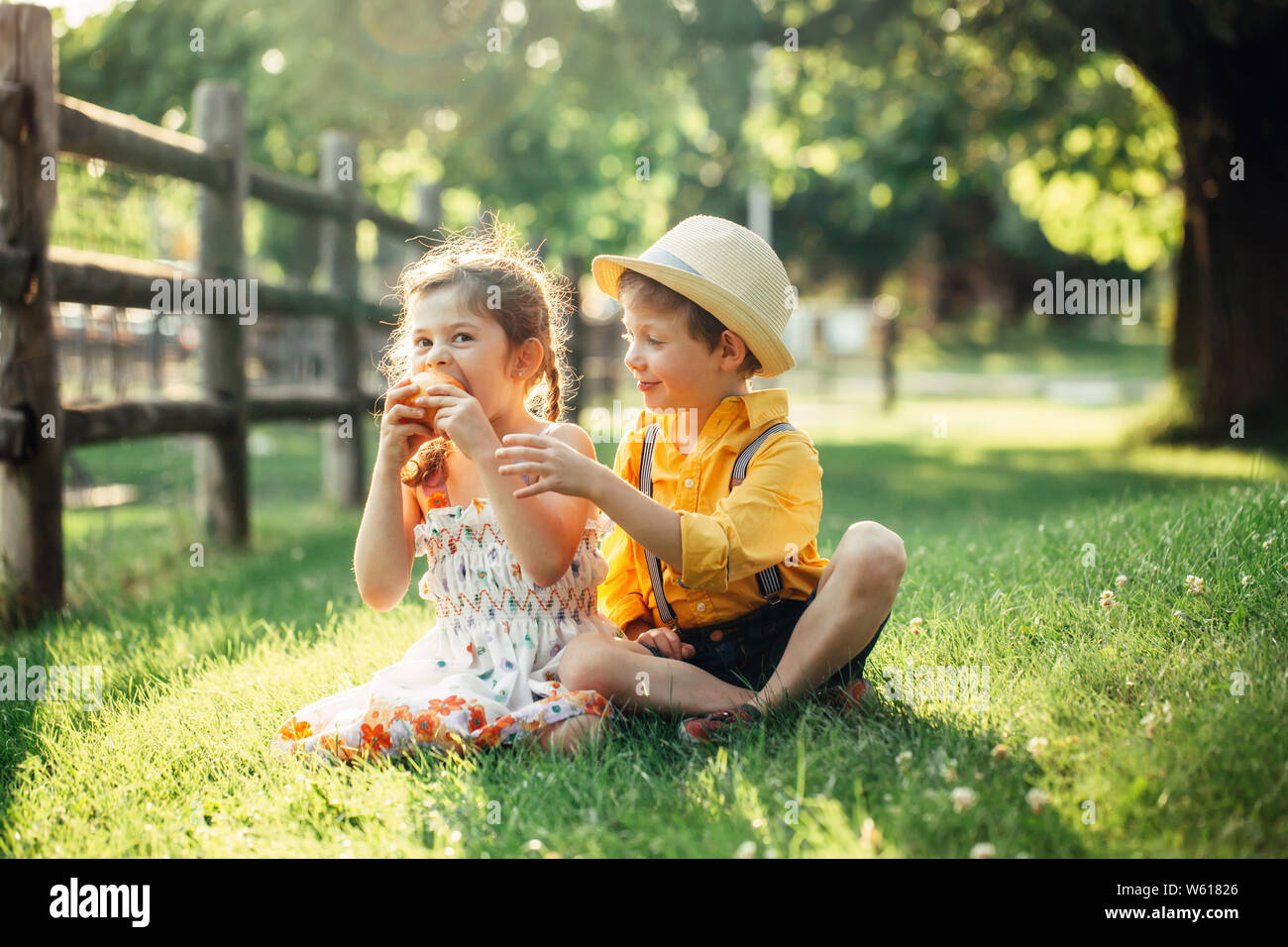 Caucasian children boy and girl siblings sitting together sharing apple ...