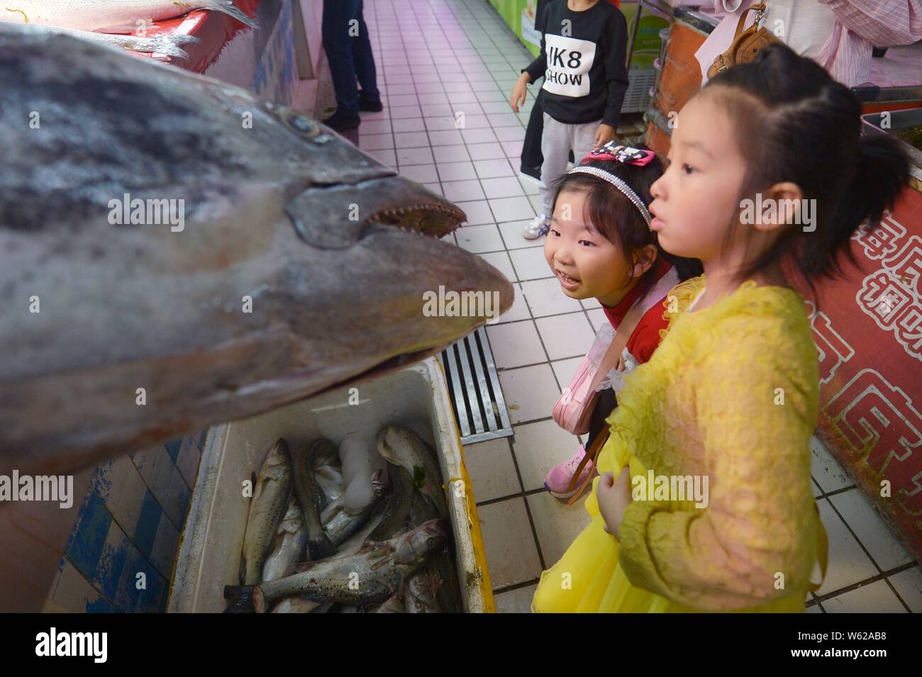 Children look at a giant Chinese seerfish for sale at a seafood market ...