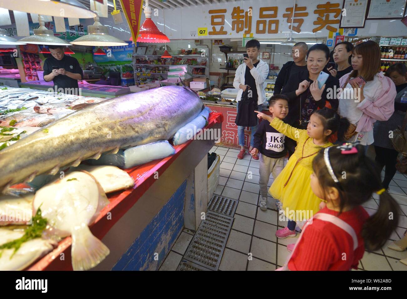 Customers look at a giant Chinese seerfish for sale at a seafood market ...
