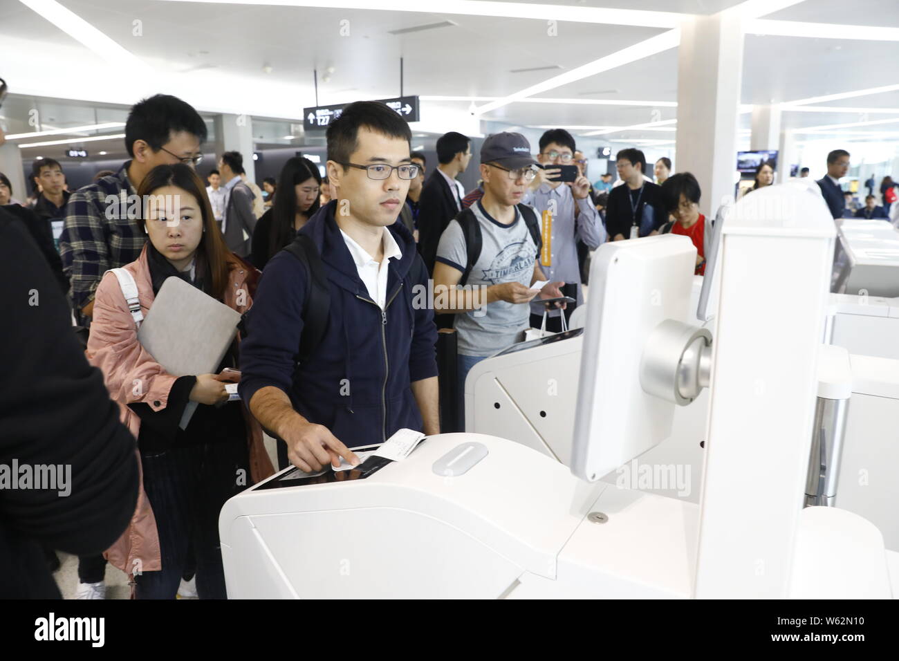 Passengers scan their boarding passes on self-service boarding machines ...