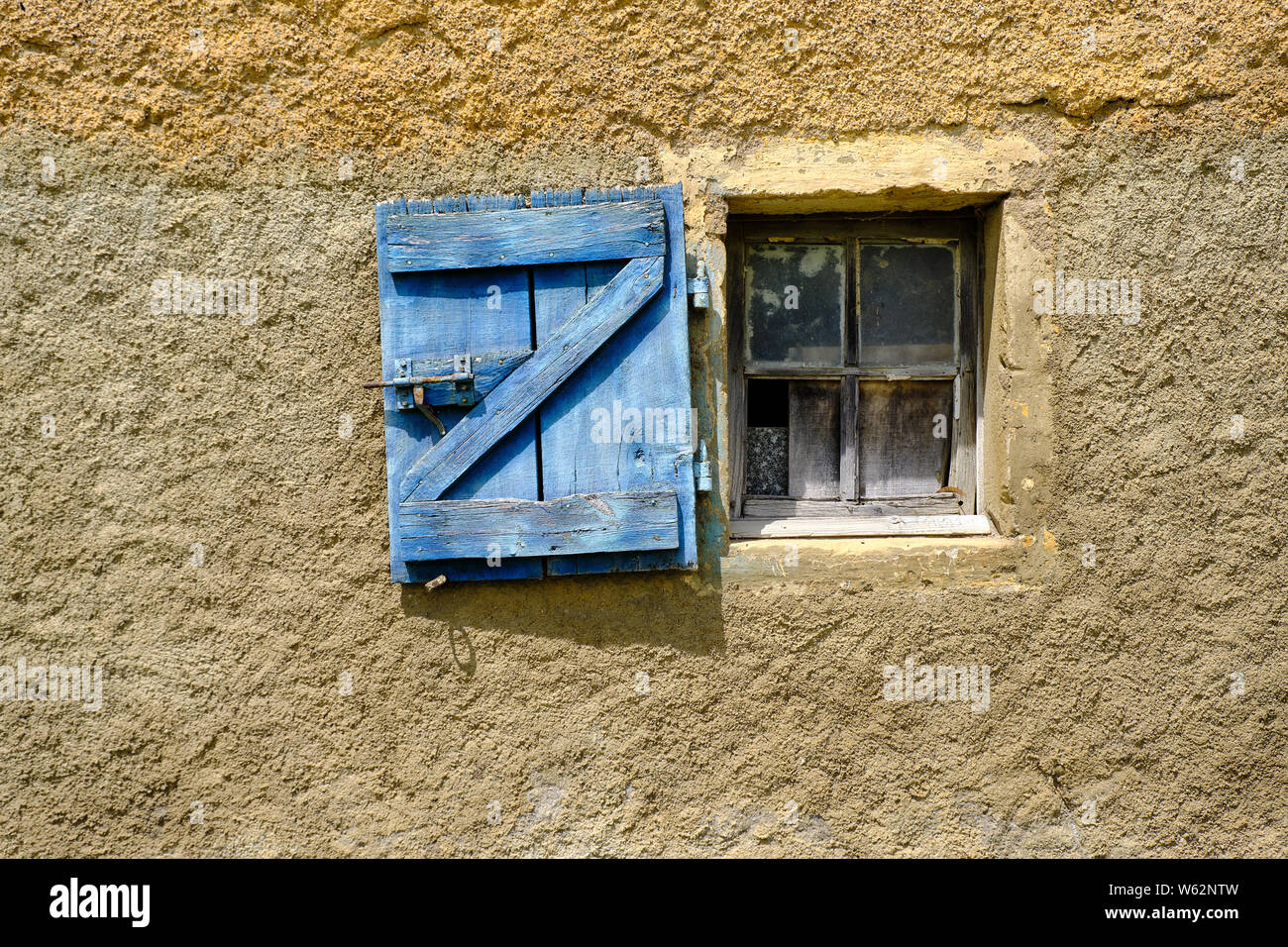 Old house window with open blue shutter in textured plaster wall ...