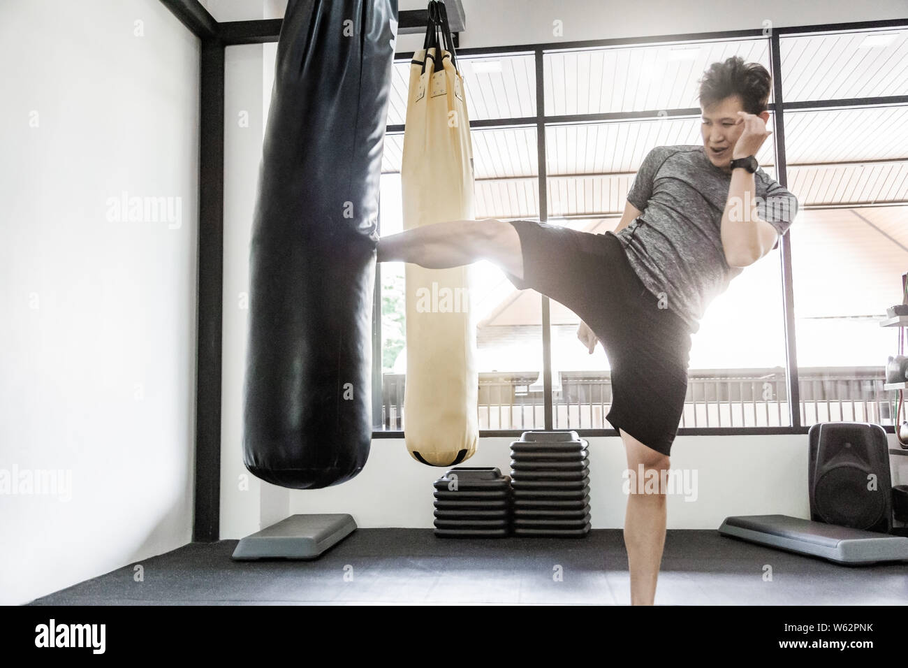 Young healthy fit Asian man practicing his kick with the punch sand bag ...