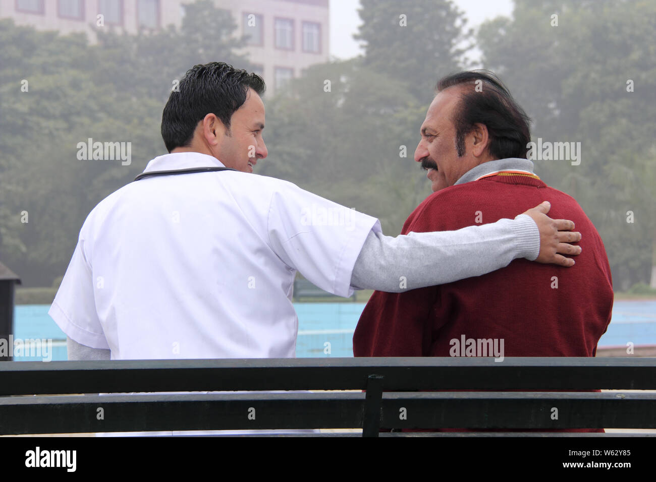 Rear view of a doctor with a patient sitting on a bench in a lawn Stock ...