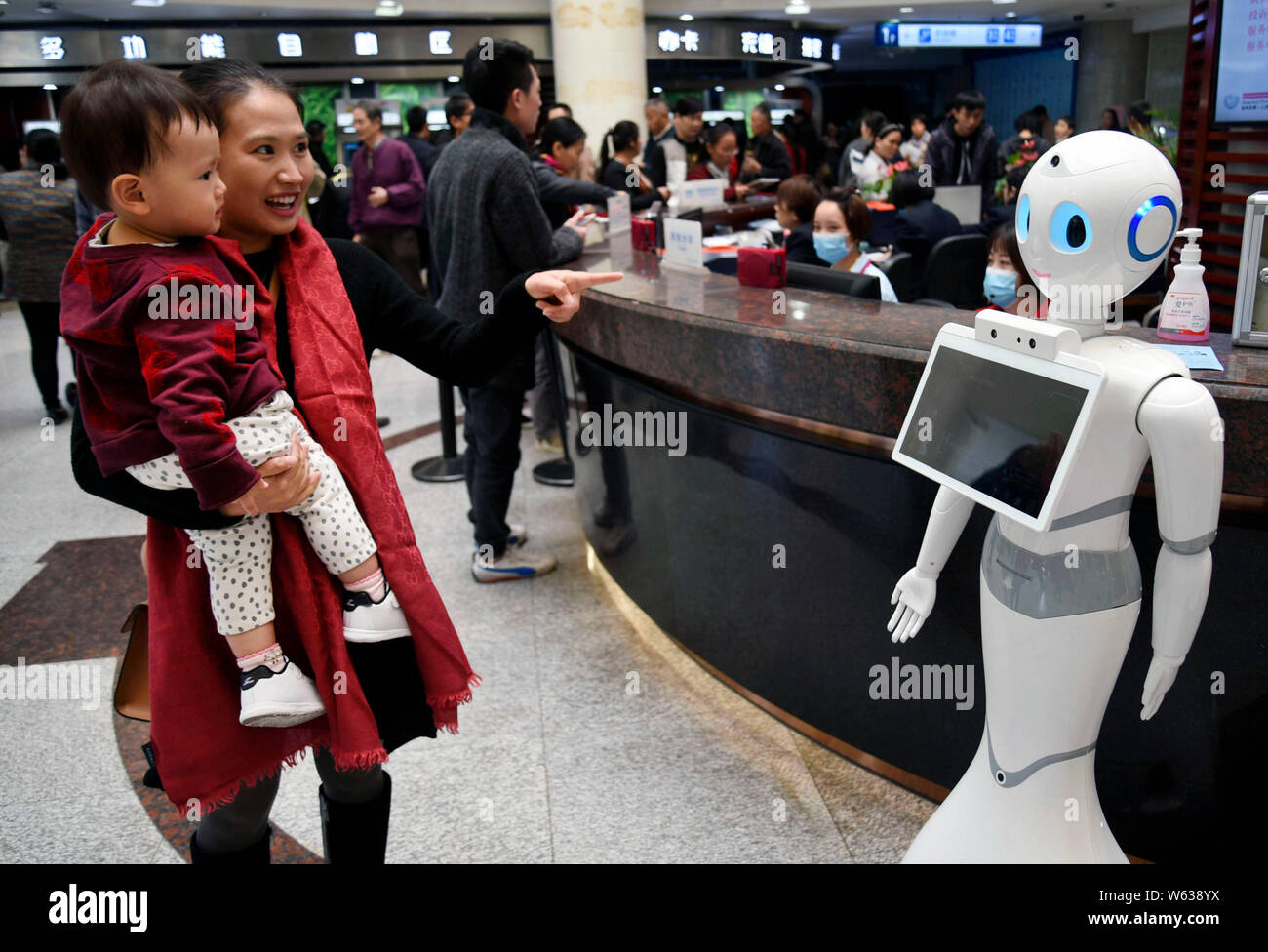 A Chinese mother holding her son looks at a robot receptionist in the ...