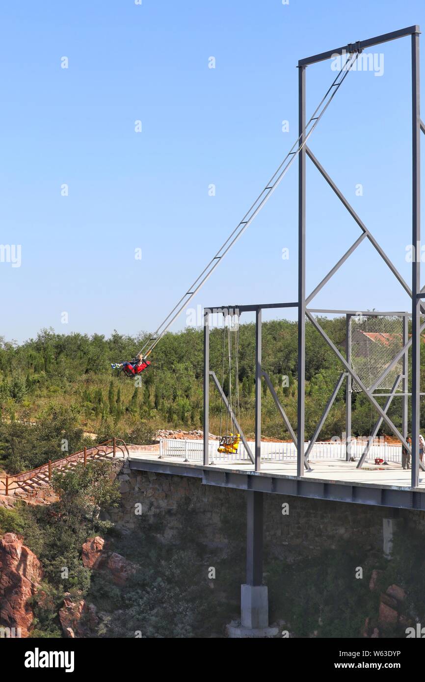 A tourist experiences a swing over the edge of a vertical cliff in a ...