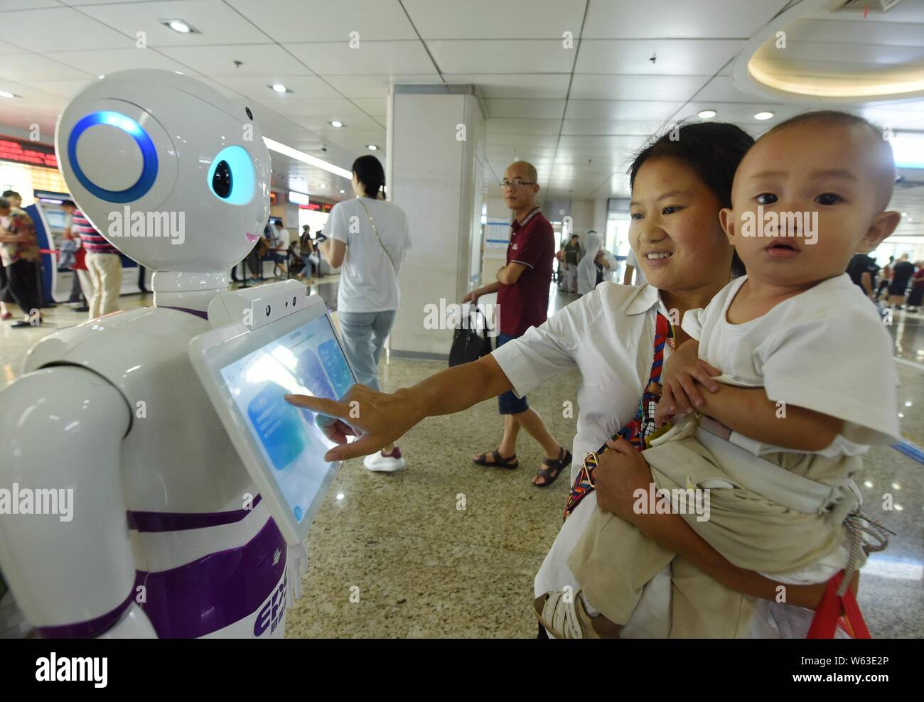 A Chinese mother holding her son interacts with a robot receptionist ...