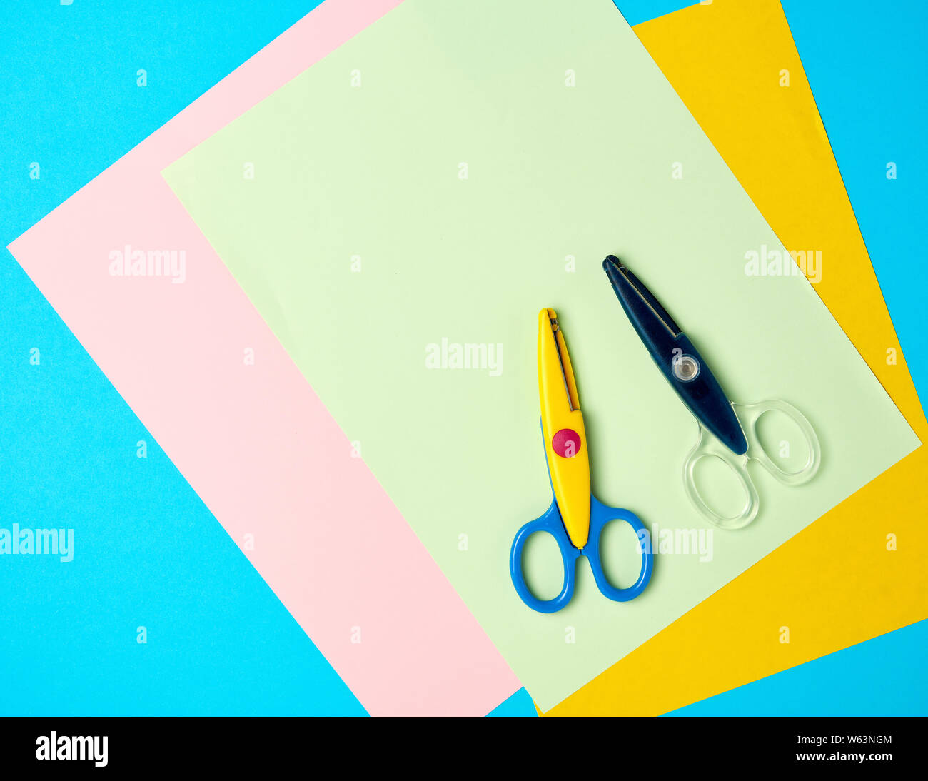 pair of plastic scissors and colored paper on a blue background, back ...