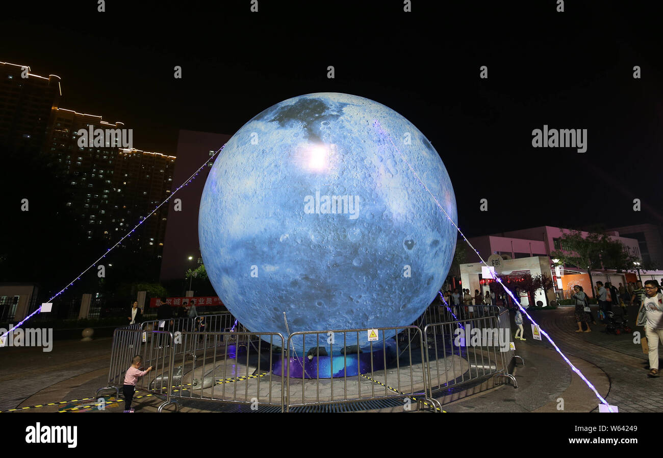 Pedestrians walk past an illuminated man-made moon in Weifang city ...