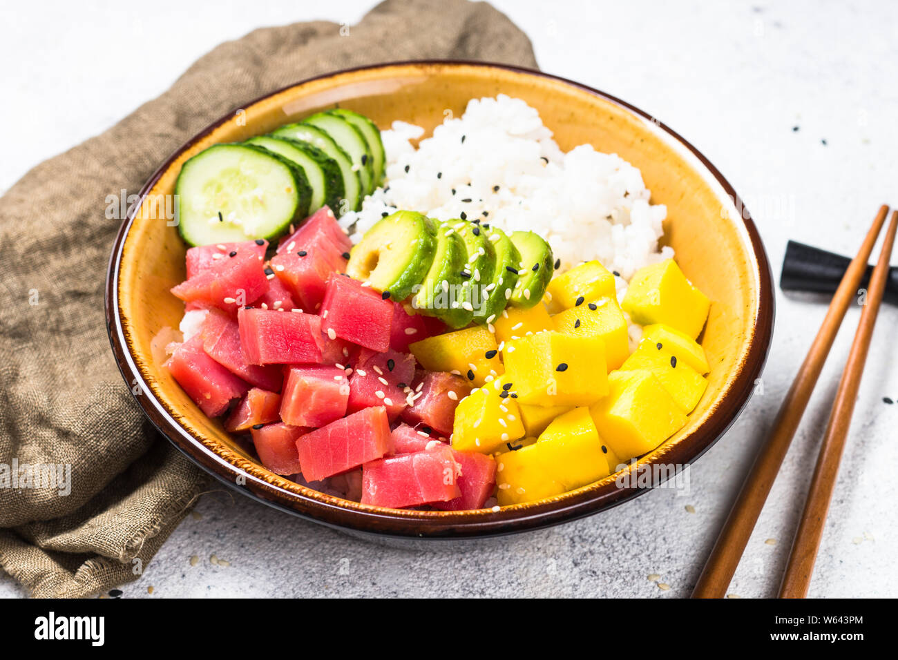 Tuna poke bowl with rice, avocado, mango and cucumber on white table ...