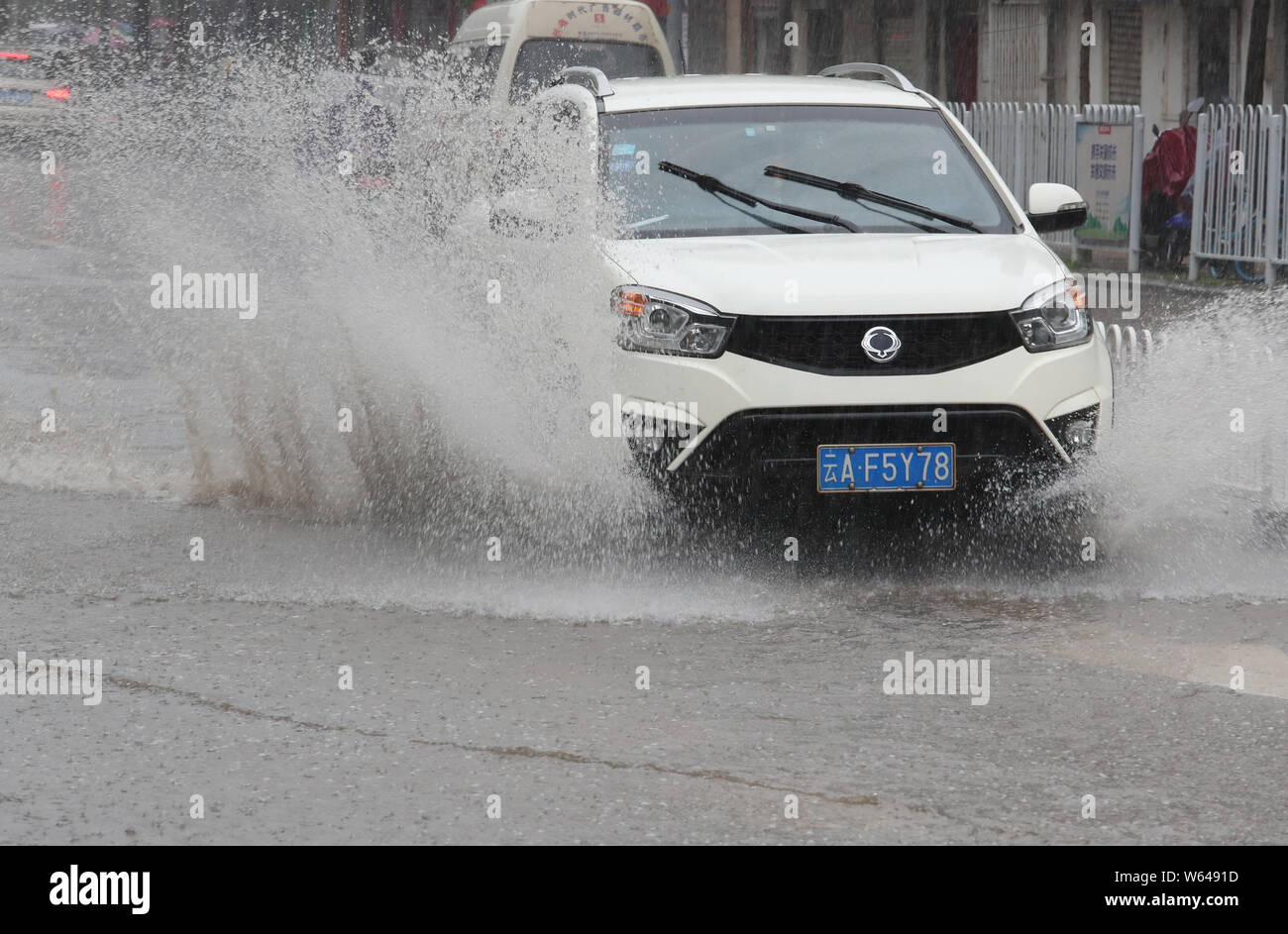 A car drives on a flooded road in heavy rainstorm and strong wind ...