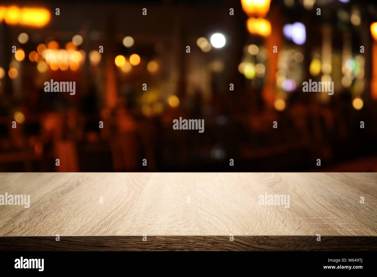 Image of wooden table in front of abstract blurred restaurant lights ...