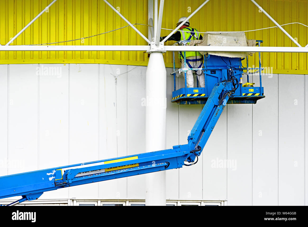 Cherry picker and male worker painting yellow and white building Stock ...