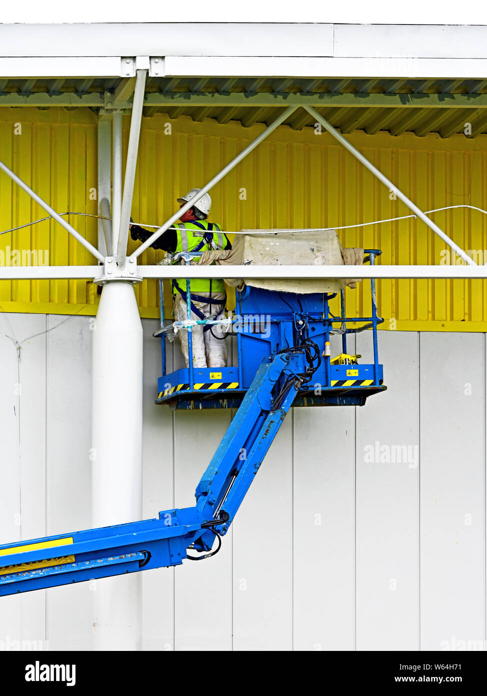 Cherry picker and male worker painting yellow and white building Stock ...