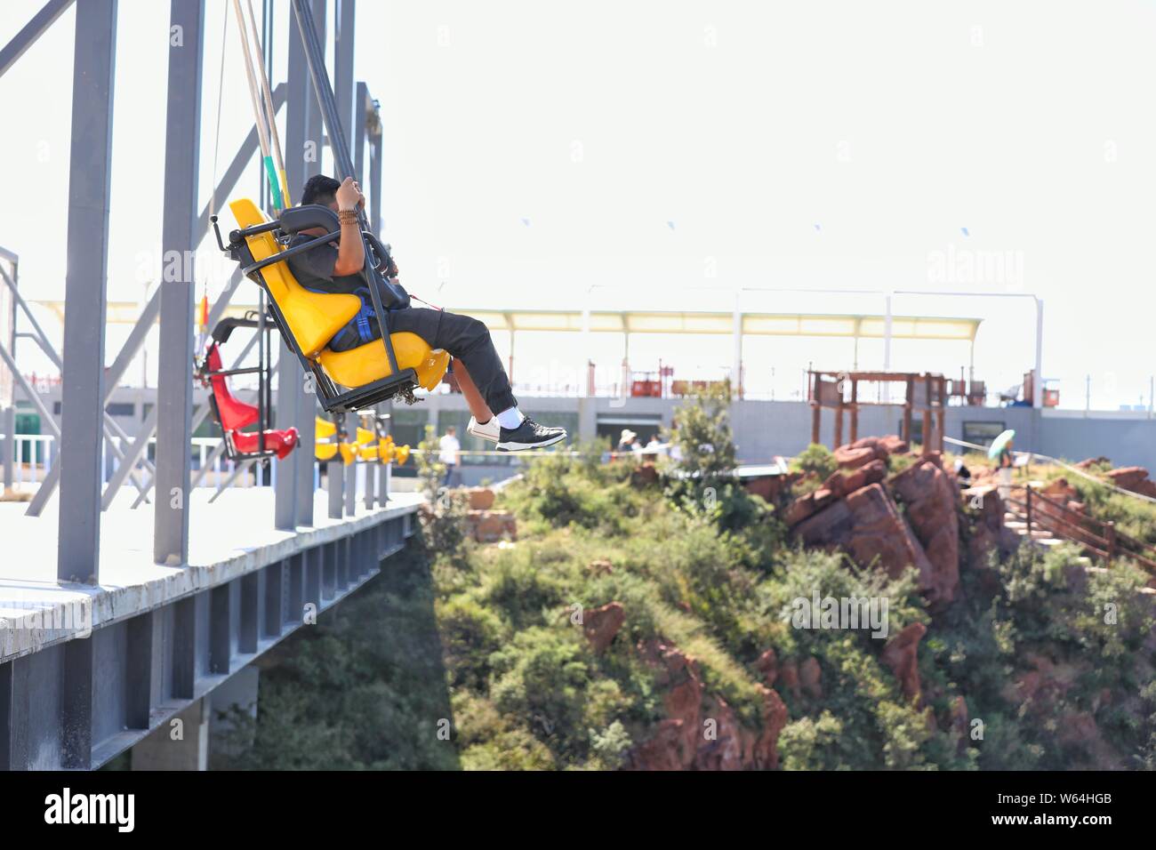 Tourists experience swings over the edge of a vertical cliff in a ...