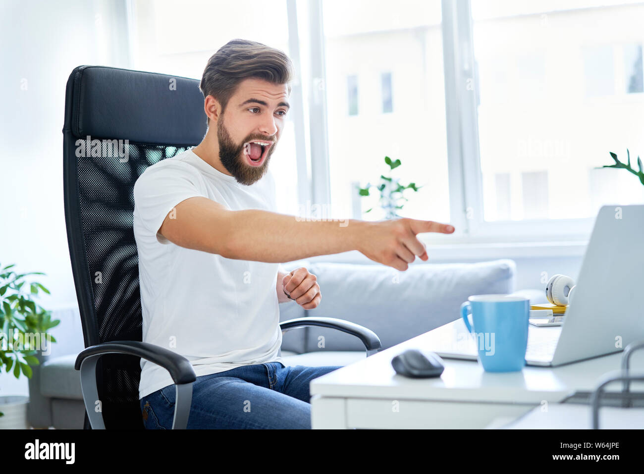 Excited young man, student pointing at his laptop sitting in dorm room ...