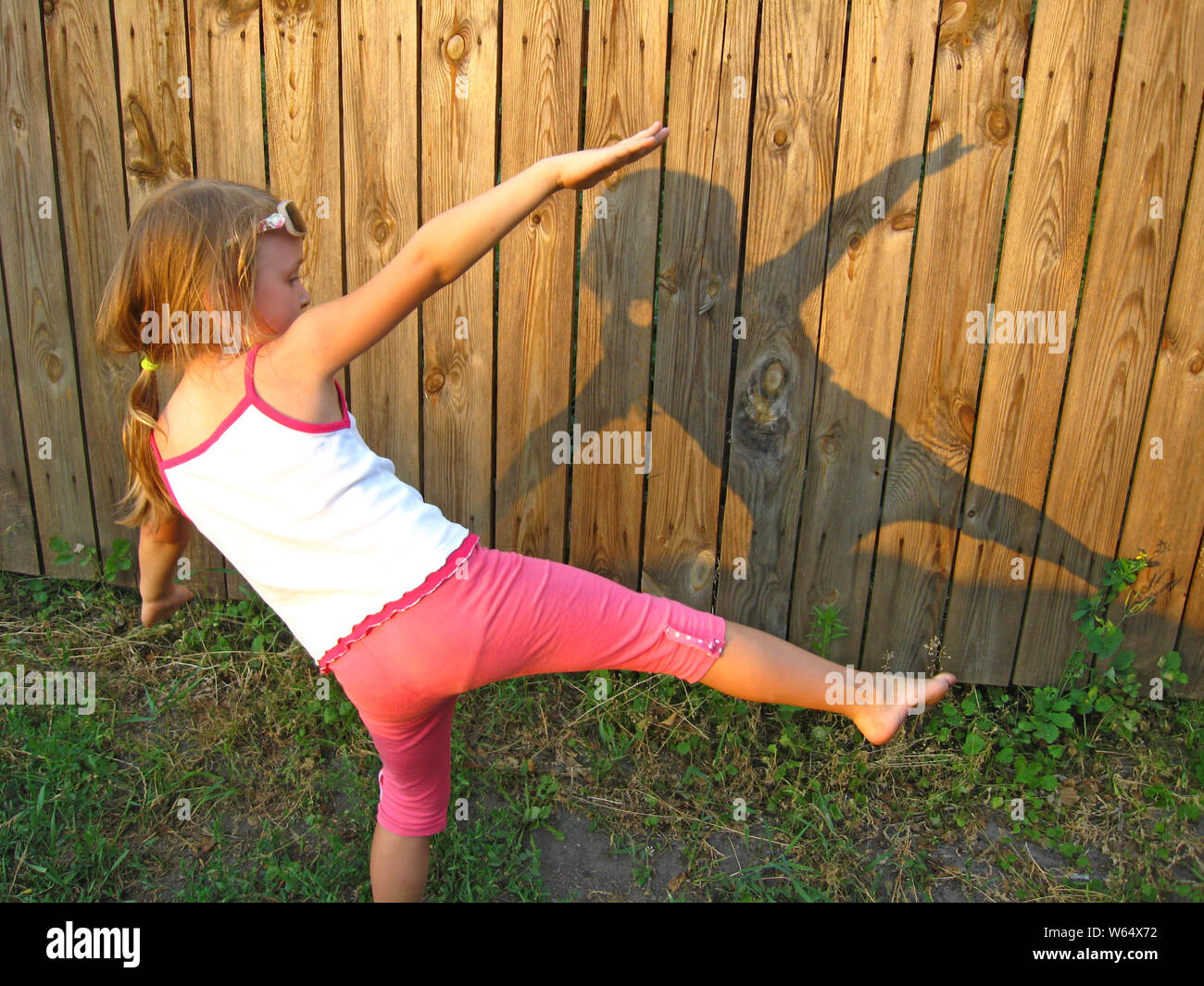 Little girl dabbling and watching shadow on fence. Child looking at her ...
