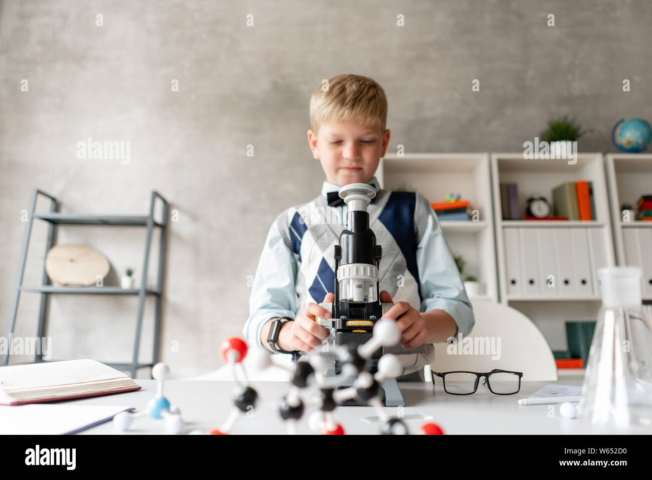 A young boy in a white shirt and sweater examines the sample under a ...