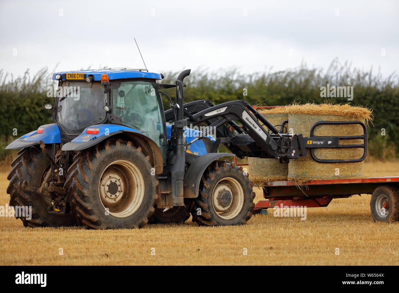 The local farmer lifting and moving his straw bales onto a trailer ...