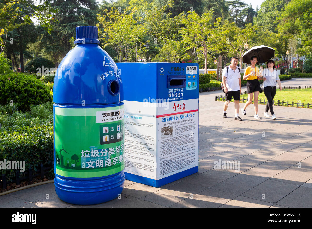Pedestrians walk bottle-shaped and carton-shaped recycling bins ...