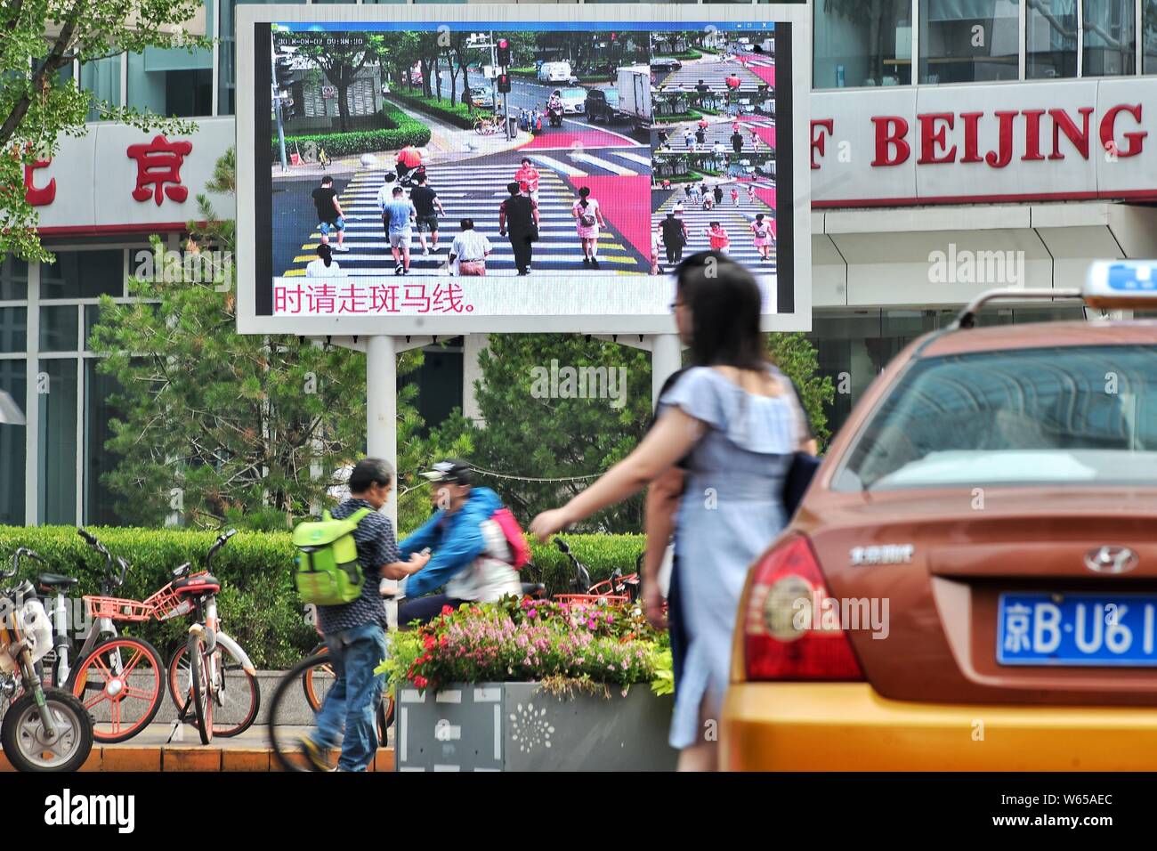 Pedestrians walk across a crossroad as a big screen supported by face ...