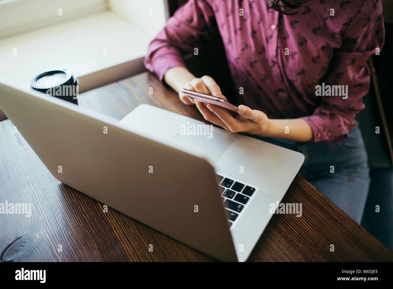 Female working with mobile phone and laptop, cup of coffee on wooden ...