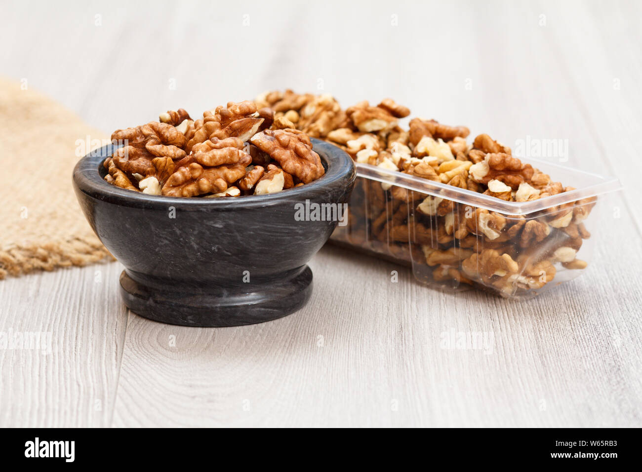 Peeled walnuts in stone bowl and plastic container on a gray wooden ...