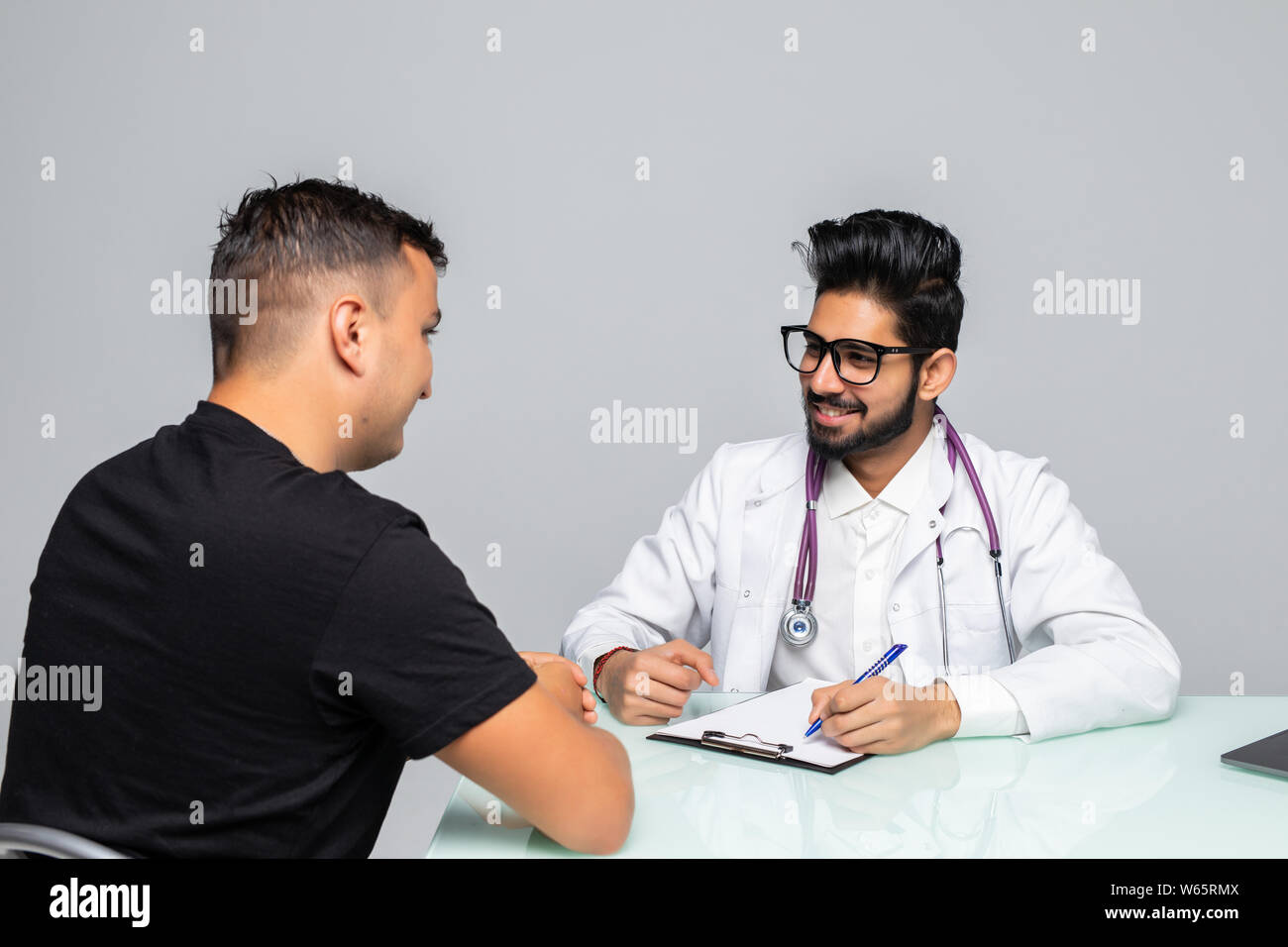 Portrait of young doctor sitting at desk with elderly patient while ...